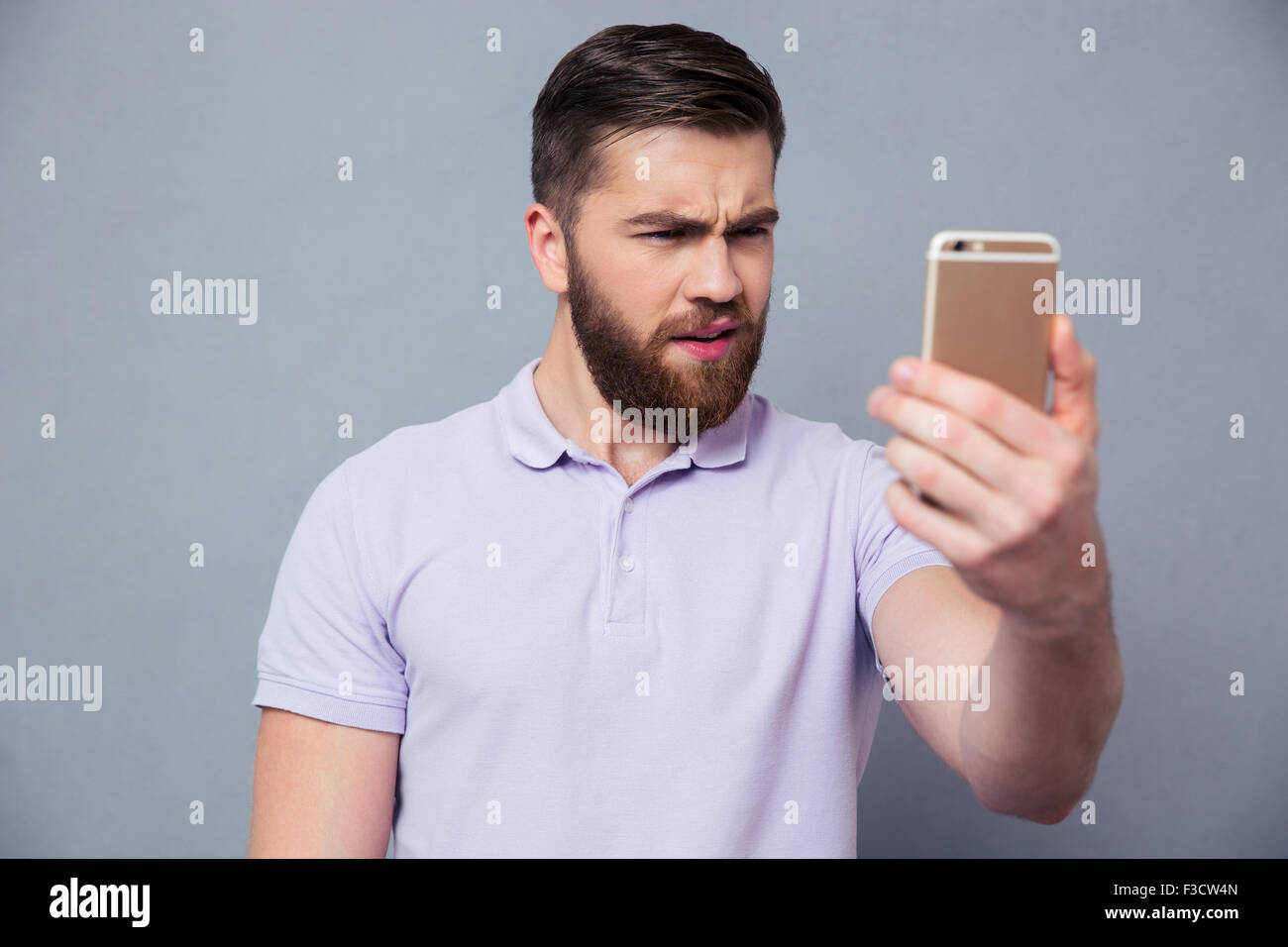 Portrait Of A Young Man Looking On Smartphone In Confusion Over Gray