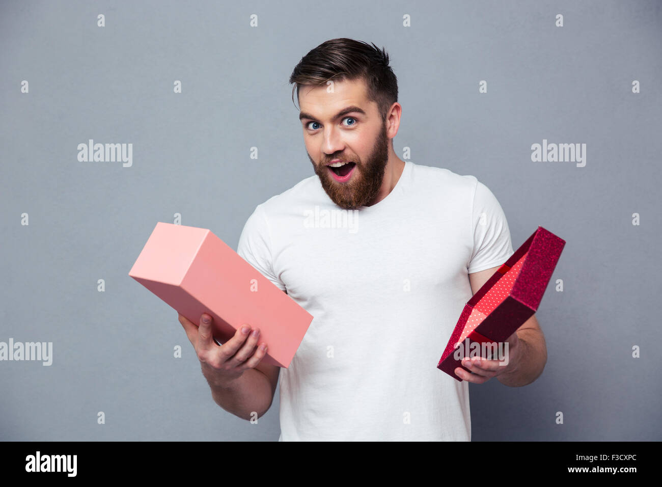 Portrait of a young man opening gift box over gray background Stock ...
