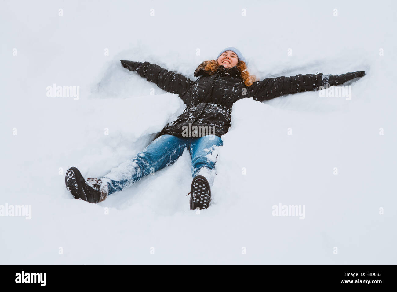 Portrait of a beautiful young woman laying down on a frozen snow lake ...