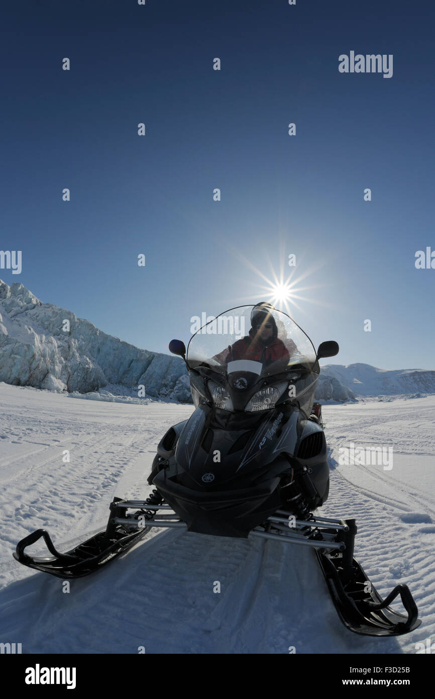 Expedition member driving with ski doo over ice from frozen sea with ...