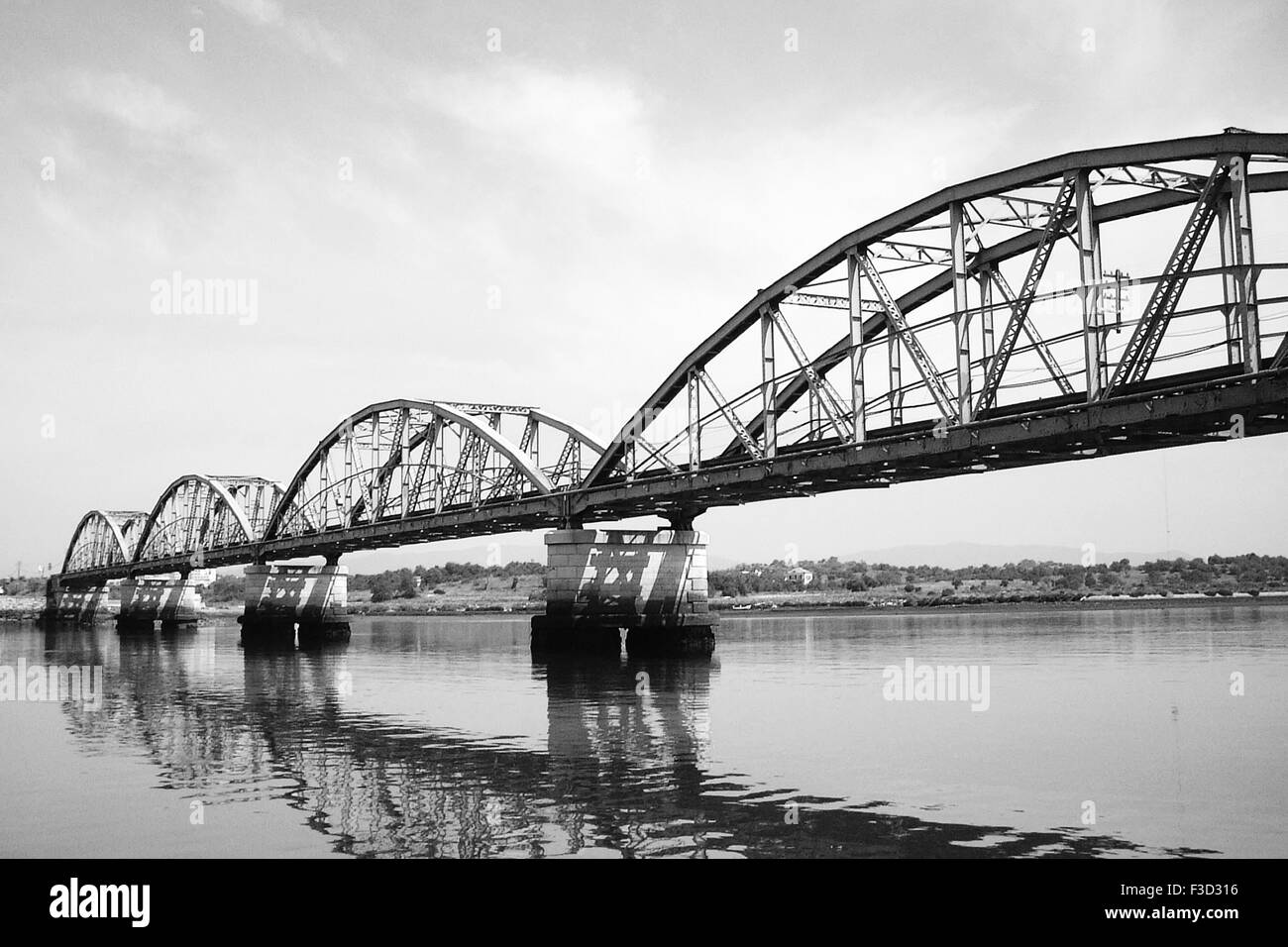 Black and white railway bridge with stone columns crossing a river ...