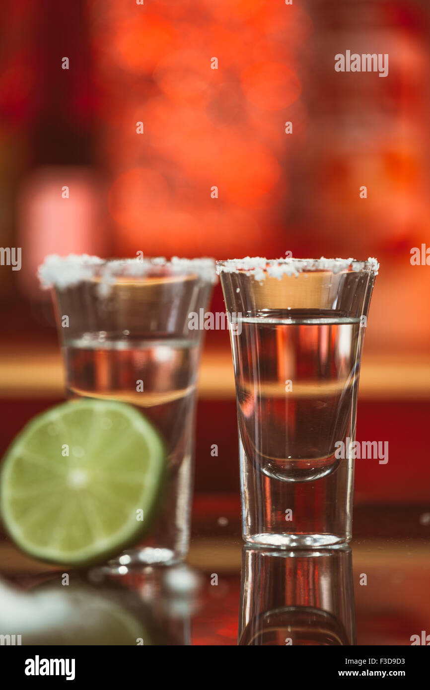 two shots of tequila with lime and salt on a wooden table bar on the ...