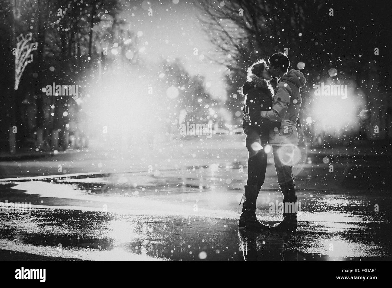 In love couple kissing in the snow at night city street black and white ...