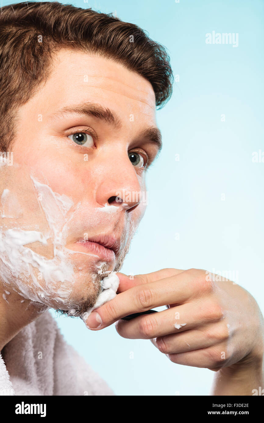 Young man shaving using razor with cream foam. Handsome guy removing face beard hair. Skin care ...