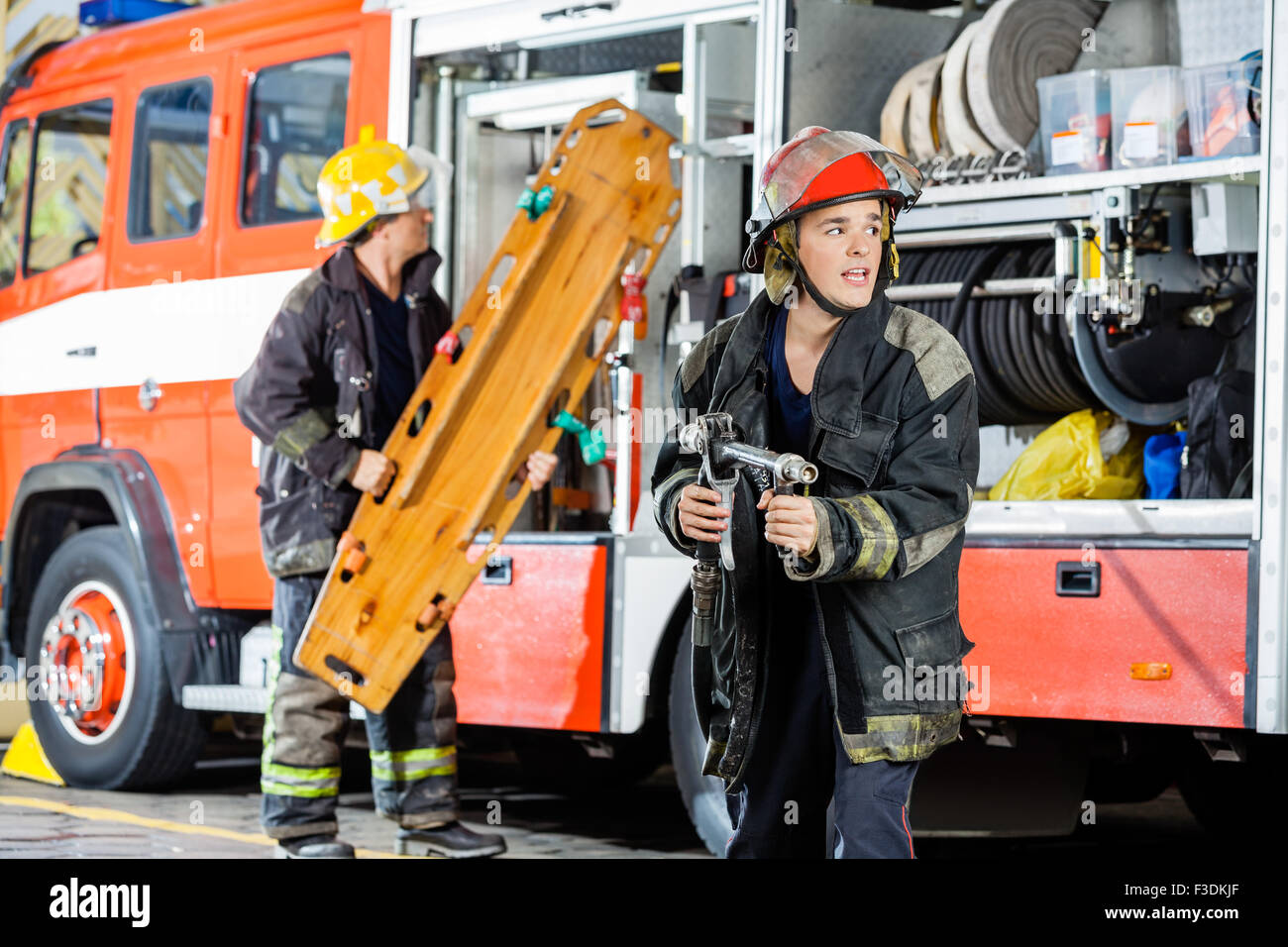Alert Firefighter Holding Hose While Colleague Carrying Wooden S Stock ...