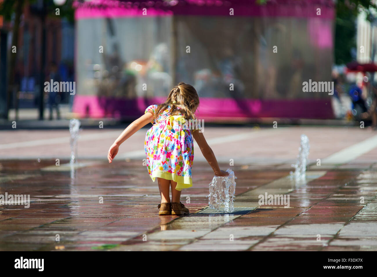 Cute little girl playing with fountain splash on the central street of ...