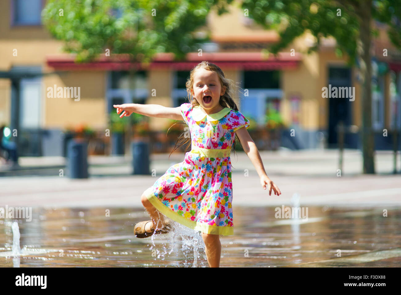 Cute little girl playing with fountain splash on the central street of ...