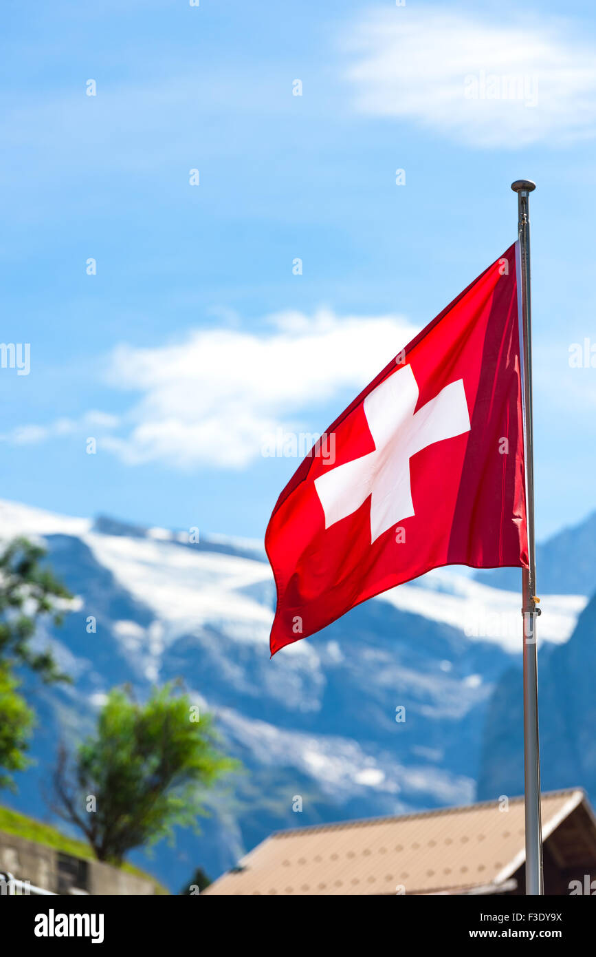 Swiss flag against Alps mountains. Vertical shot with a selective focus ...