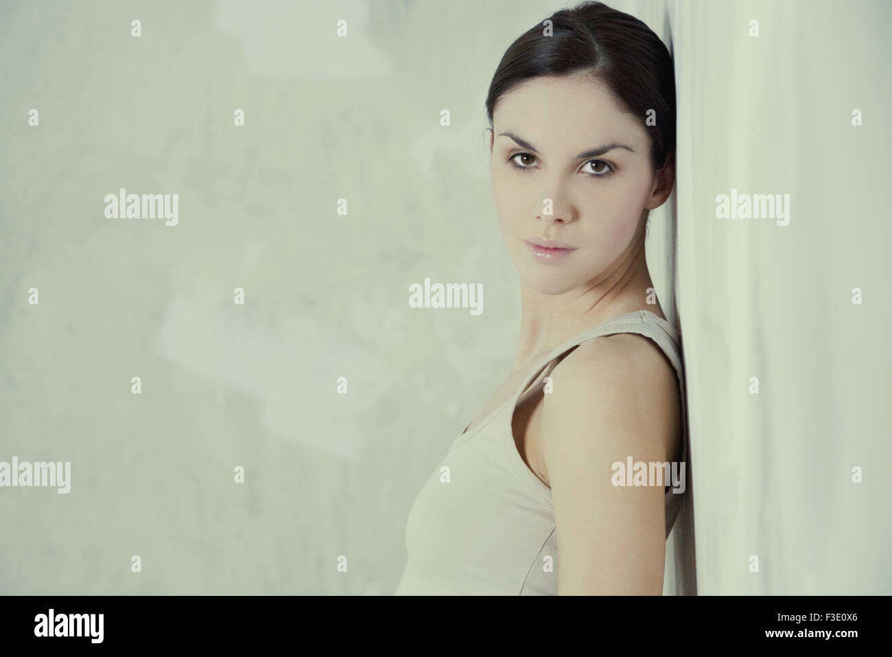 Young woman leaning against wall, looking over shoulder at camera Stock ...
