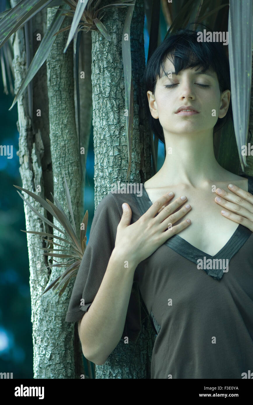 Woman leaning against palm tree, eyes closed, hands on chest Stock ...