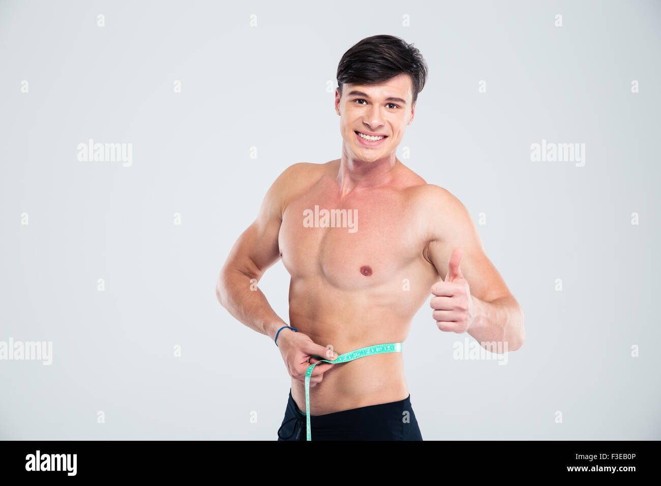 Portrait of a smiling fitness man measuring his body and showing thumb ...