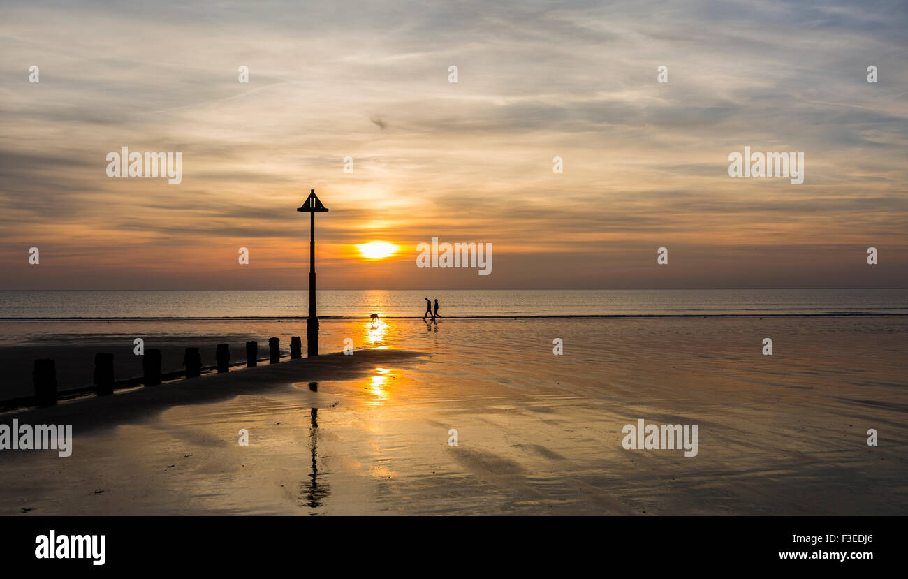 The sunset at Borth beach with walkers silhouetted against the skyline ...