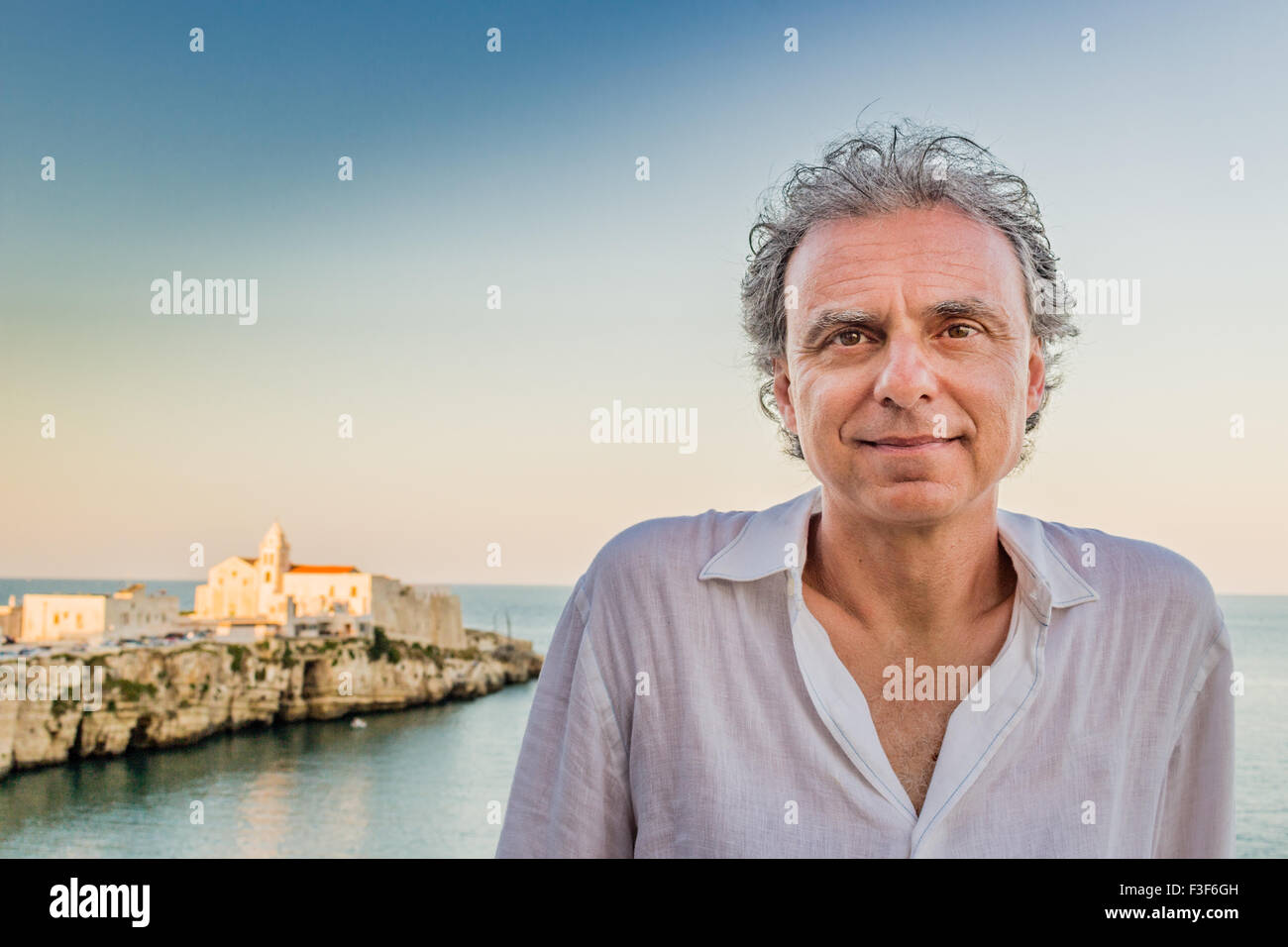 charming middle-aged man in white shirt in a seaside ancient Italian ...