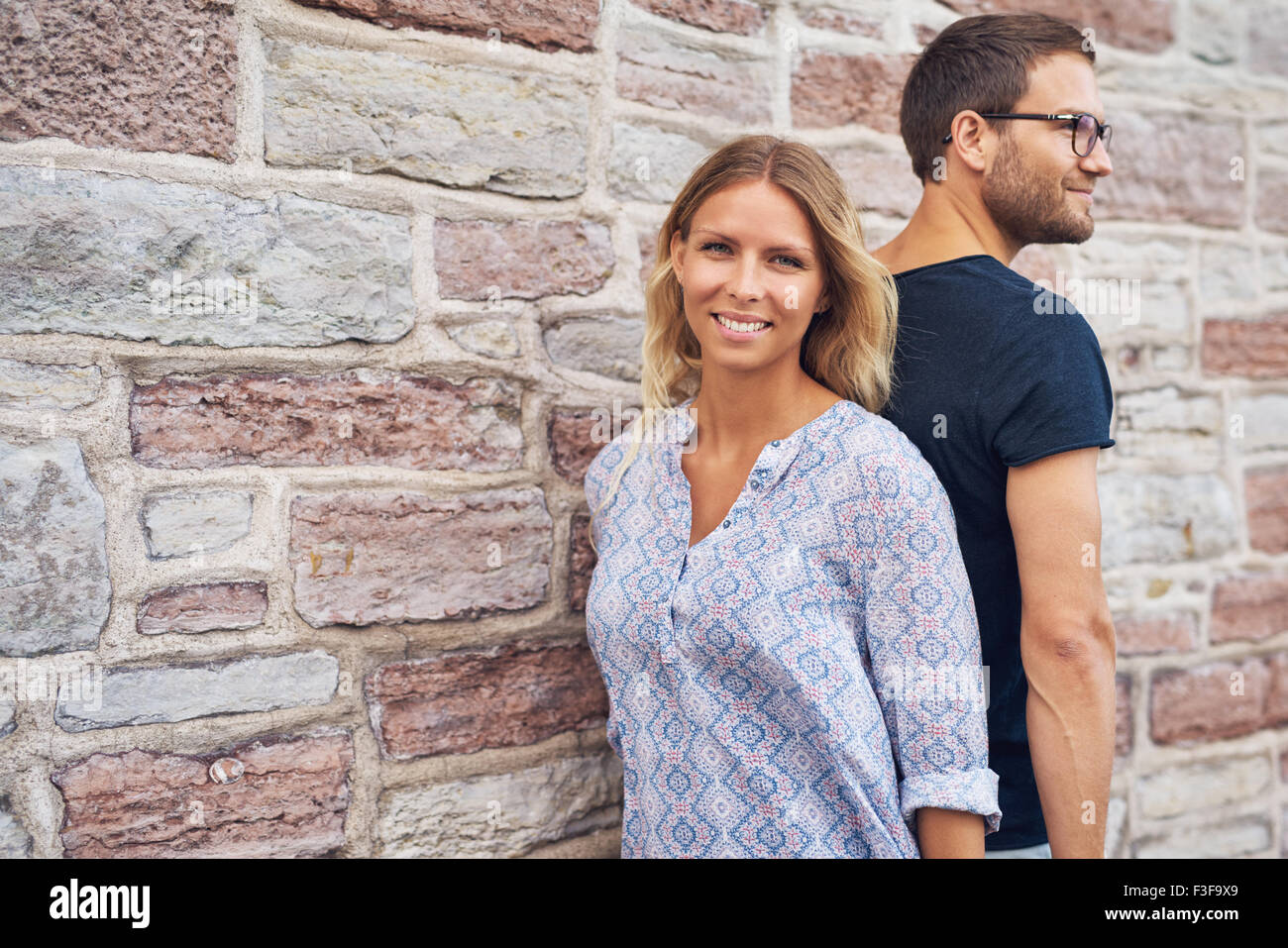 Couple standing back against each other against a wall Stock Photo - Alamy