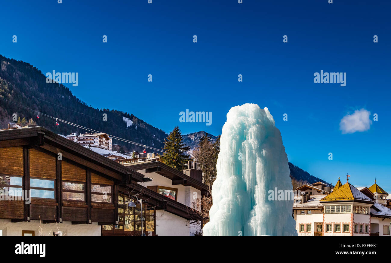 Frozen ice fountain in snowy alpine village in Italy illuminated by sun ...