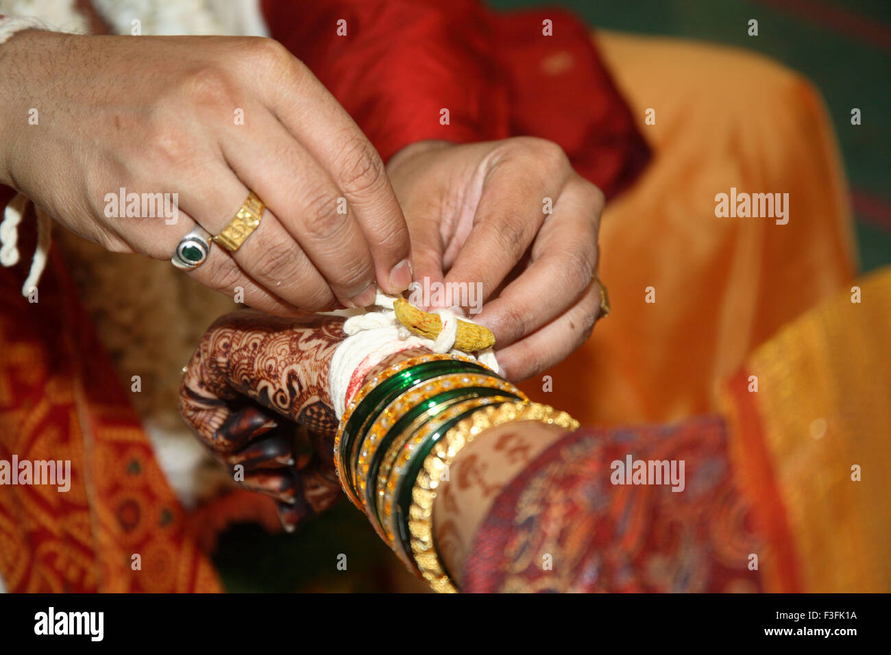 Bridegroom tying kankan or halkund with thread on wrist of bride ...