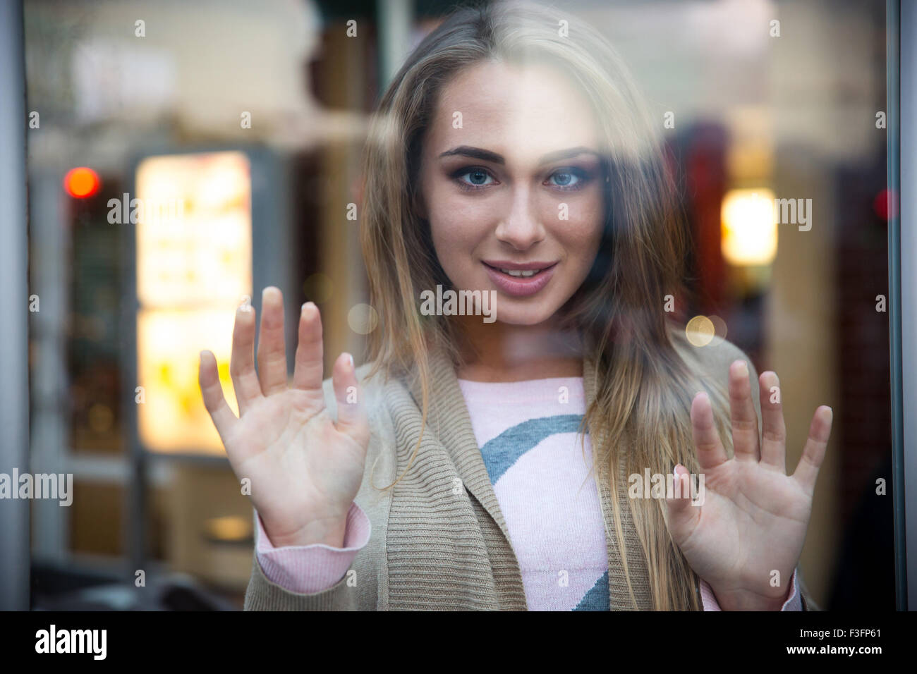 Portrait of a beautiful young woman looking at camera through window ...
