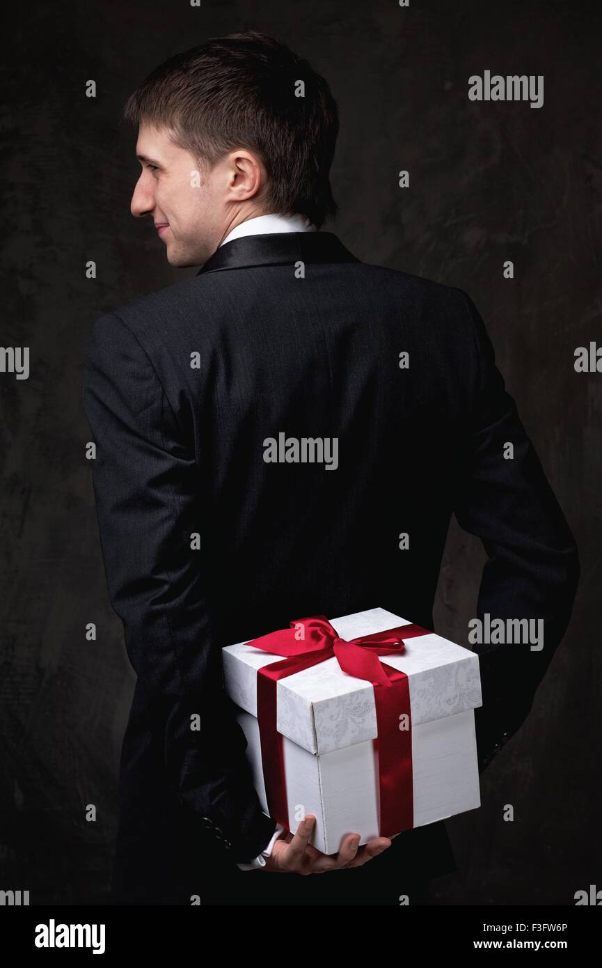 Young man hiding a gift box behind his back Stock Photo - Alamy