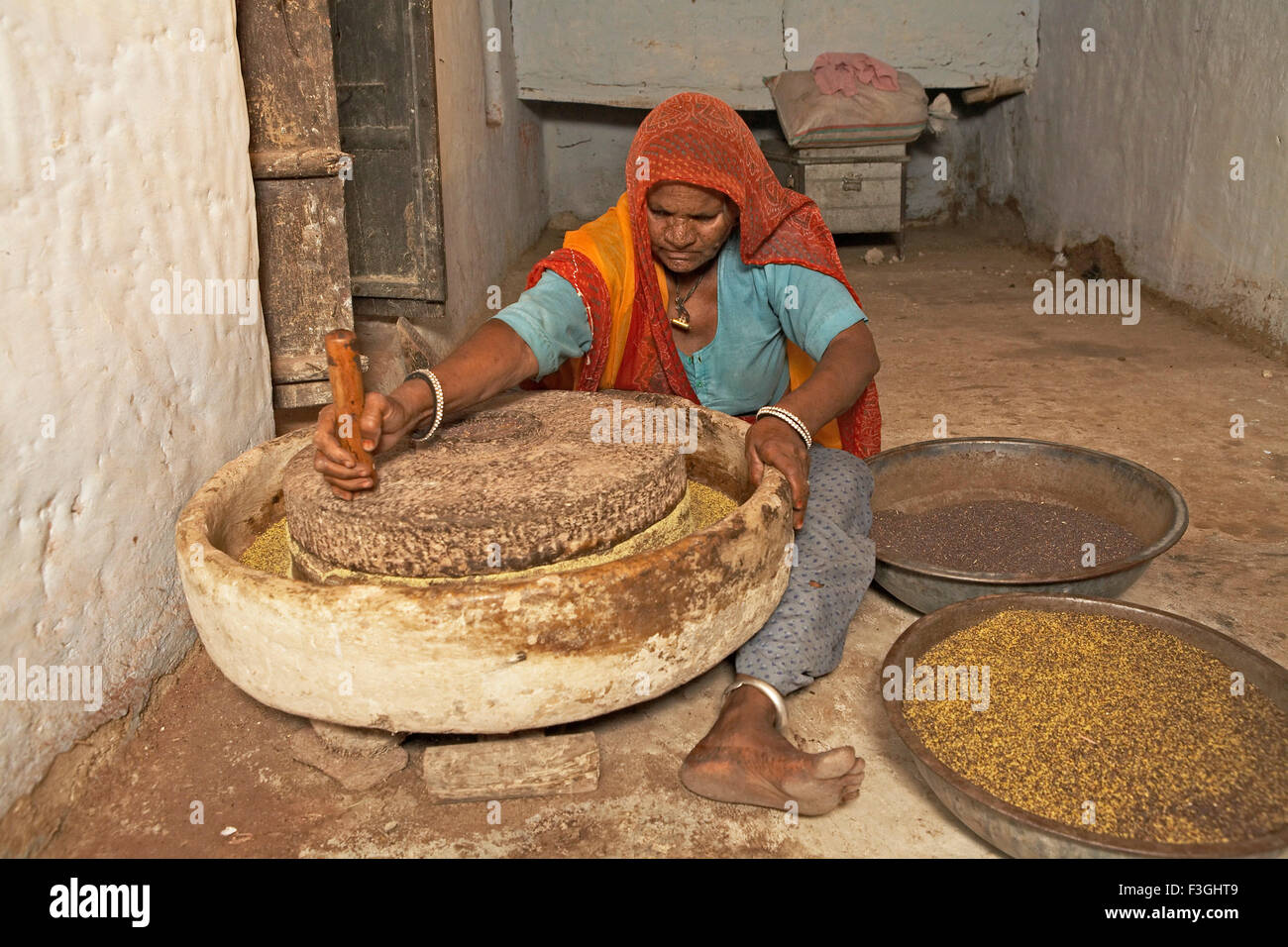 A woman using stone grinding wheel to split mustard seed before putting ...