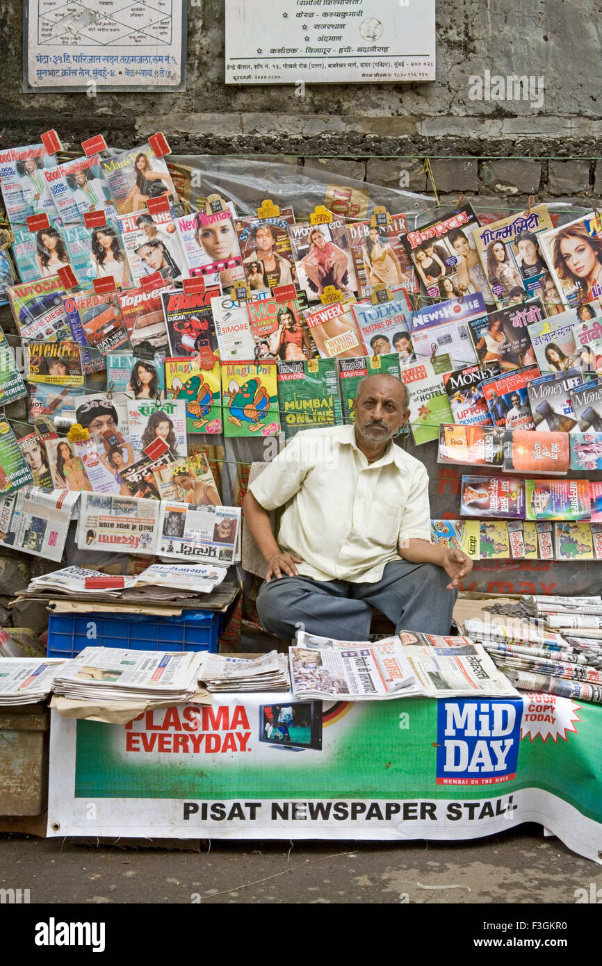 A newspaper vendor amidst his display of newspapers and magazines on ...