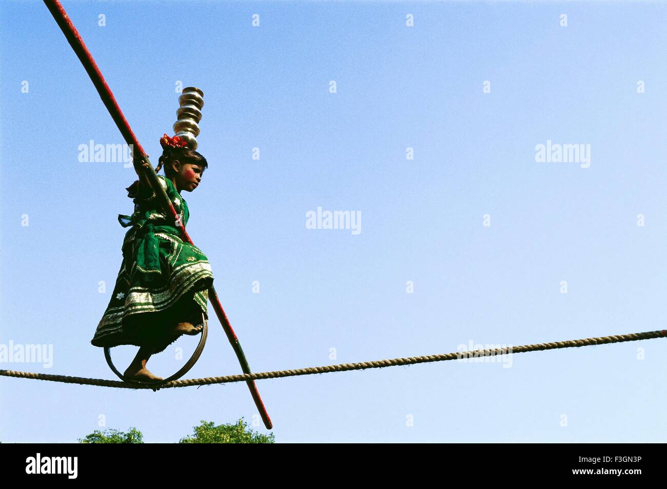 Girl showing balancing act by walking on rope with bamboo in hand ...