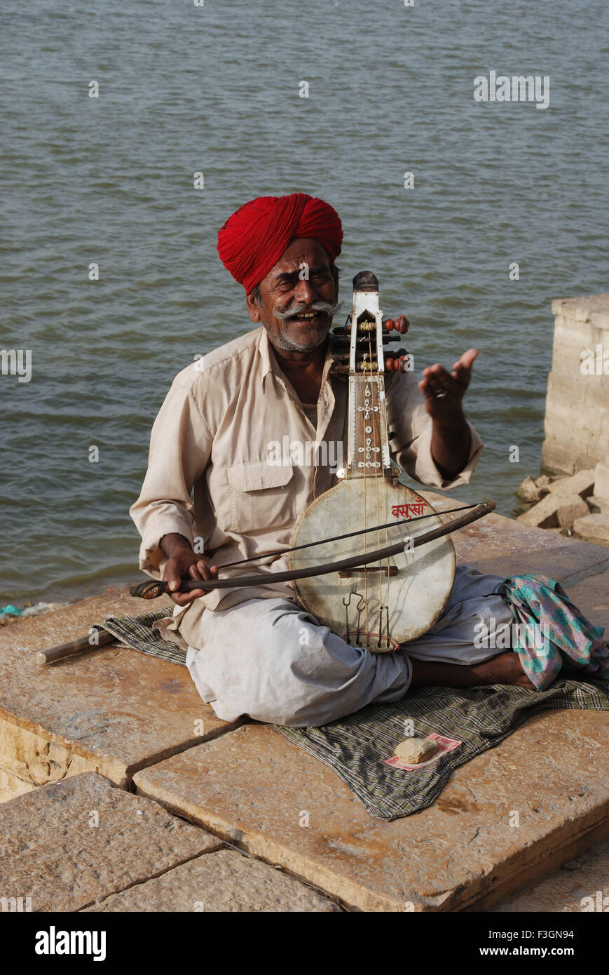 Folk singer singing and playing musical instrument at Gadisar lake ...