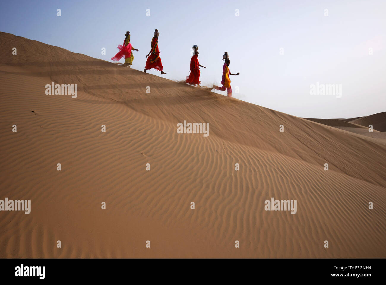 Girls with pitcher coming down dune; Khuhri ; Jaisalmer ; Rajasthan ...