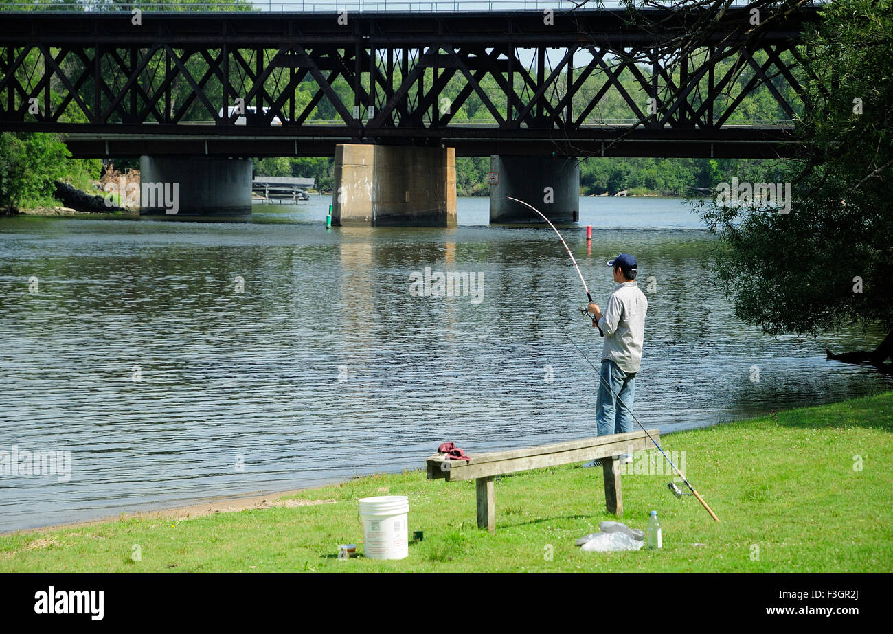 Man fishing from shoreline near river bridge Stock Photo - Alamy