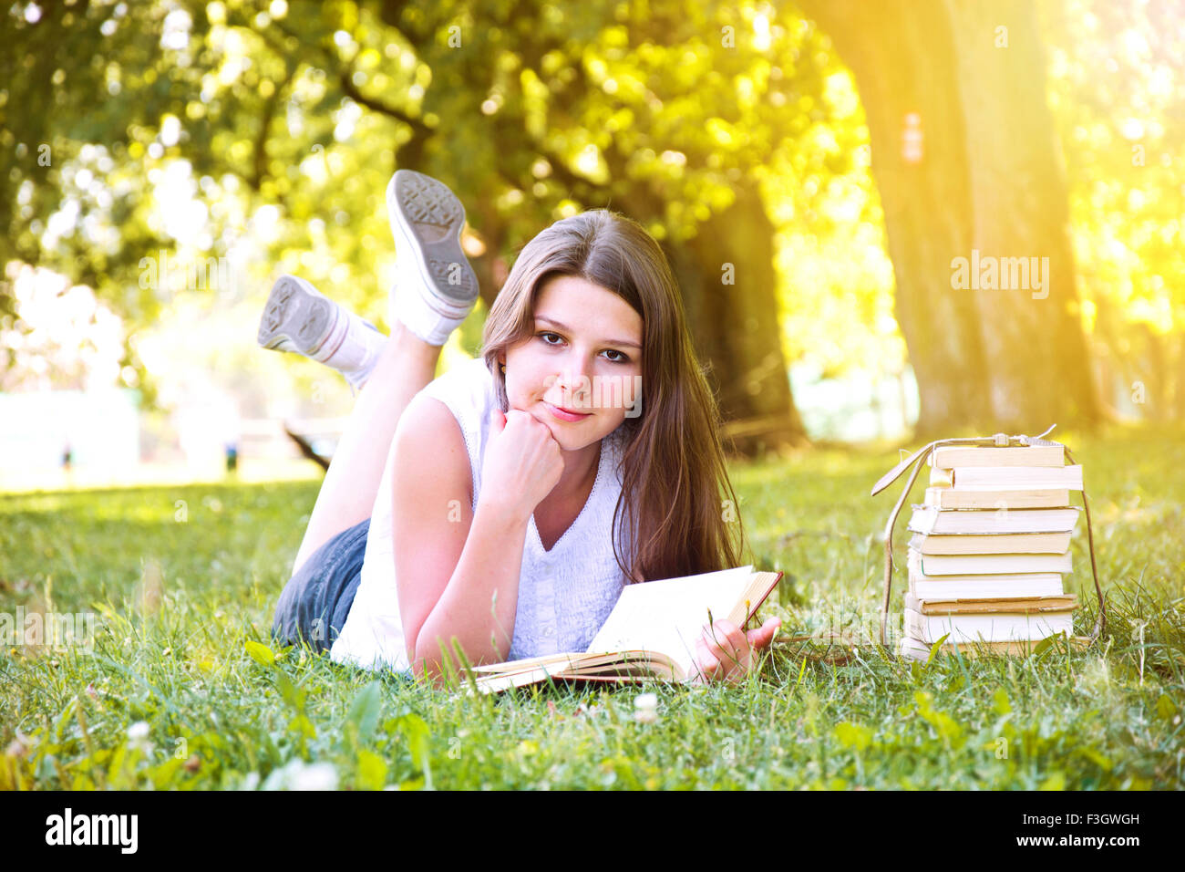 Young beautiful college student girl lying down on the green grass and ...