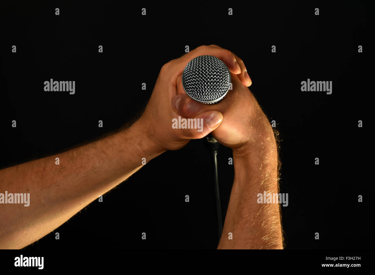 Two male hands holding microphone with wire cable isolated on black ...
