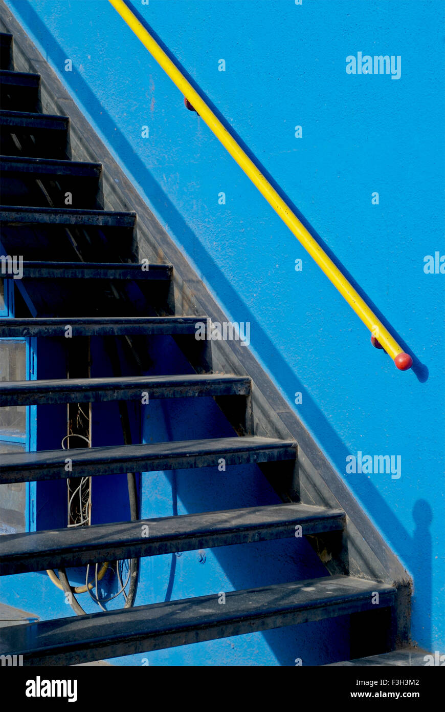 Black stair case of a building with blue walls and a yellow railing at ...