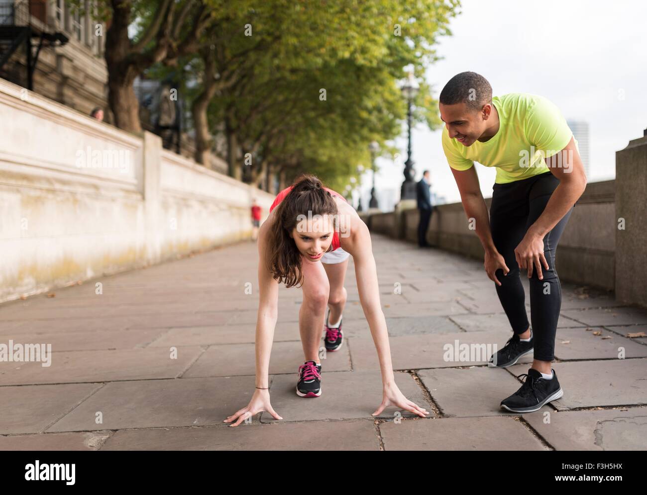 Young male trainer practicing starts with female runner on riverbank ...