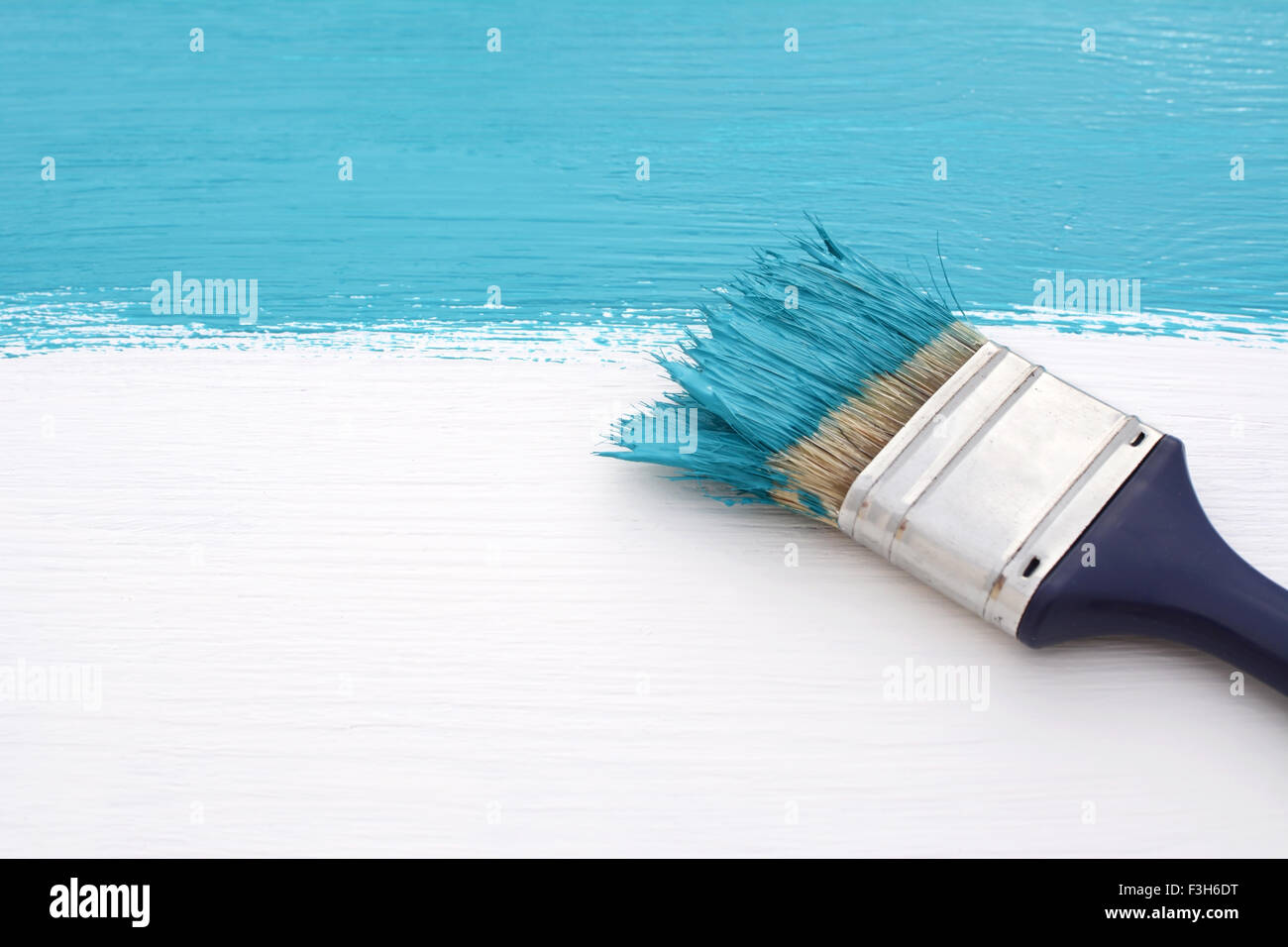 Paintbrush loaded with bold blue paint, painting over white wooden ...