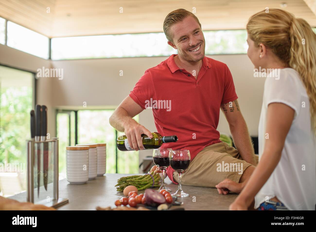 Couple preparing food and pouring red wine in kitchen Stock Photo - Alamy