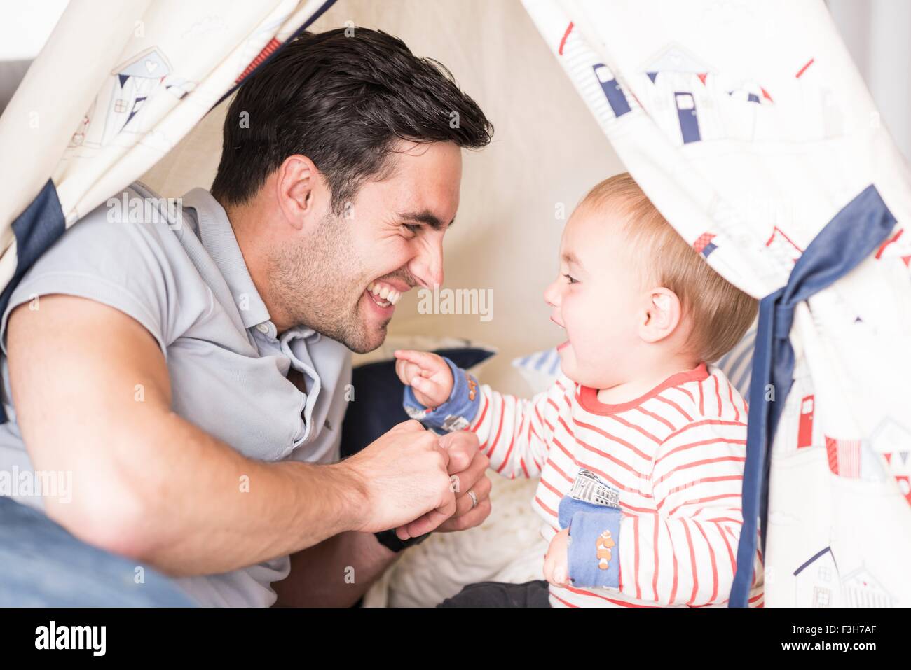 Father and young son sitting in play tent indoors, laughing together ...