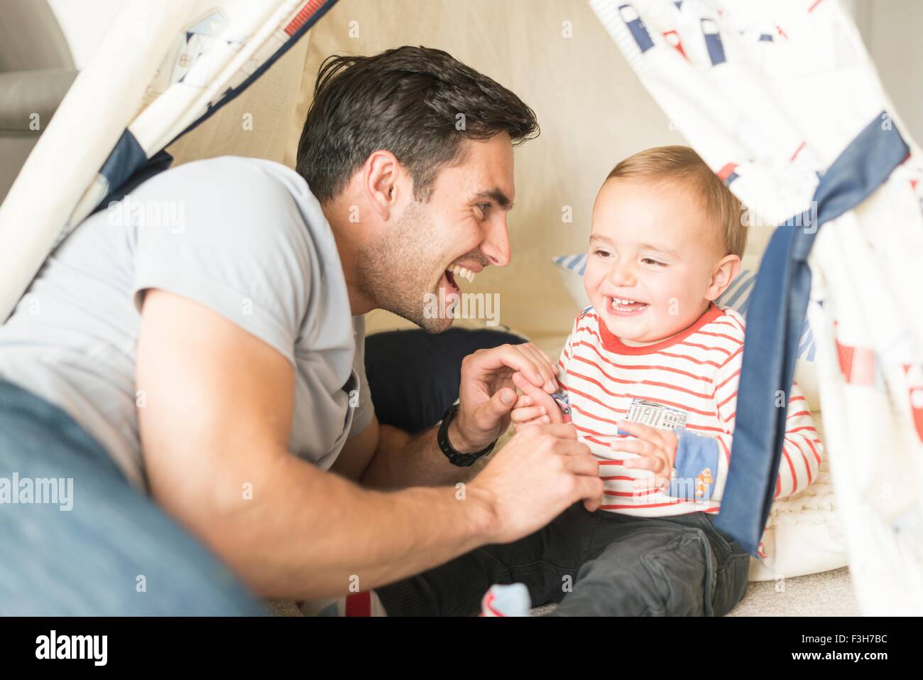 Father and young son sitting in play tent indoors, laughing together ...