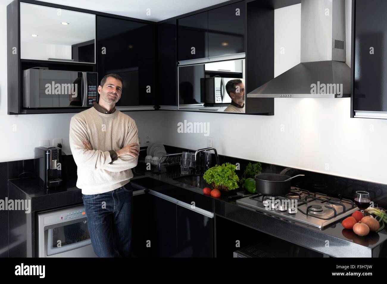 Mature man standing in kitchen leaning against counter arms folded ...