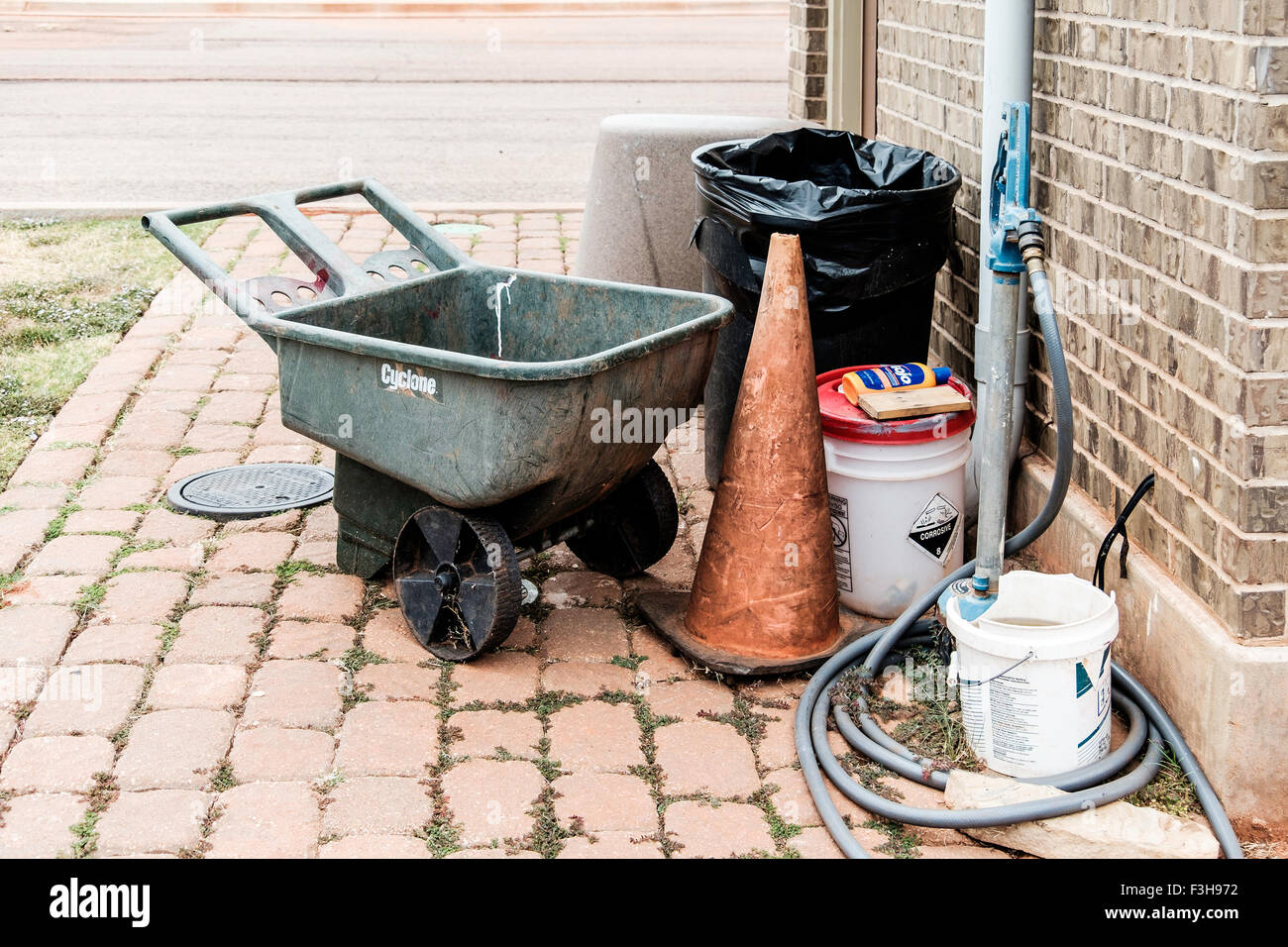 A utility cart,orange parking cone,garbage bin and hose gathered next ...