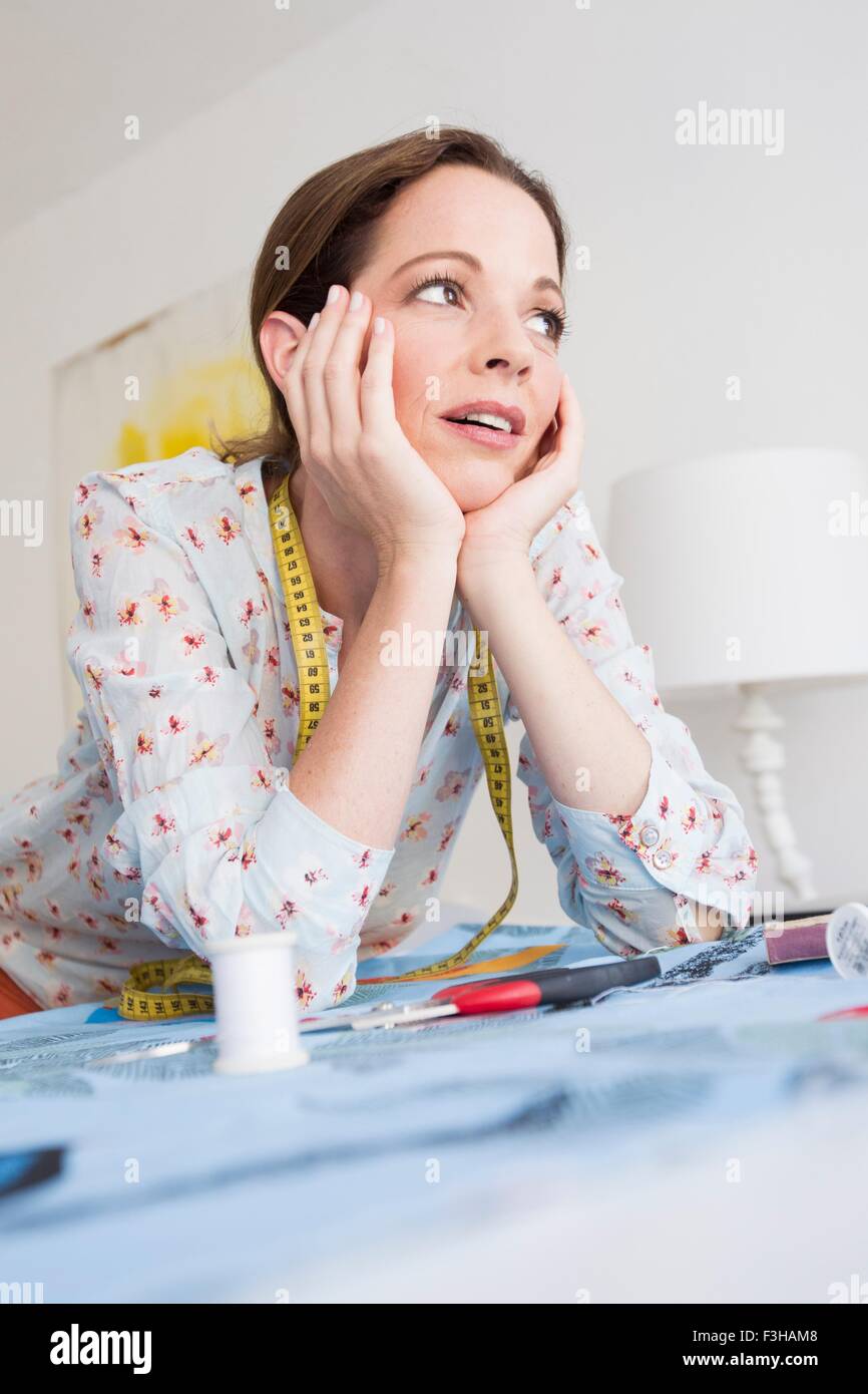 Mature woman with tape measure resting on elbows, chin on hands looking ...
