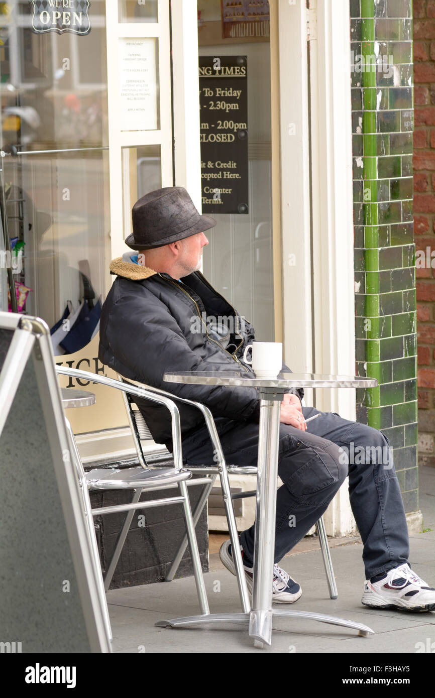 Man sat smoking at table with coffee cup outside cafe in Bedford ...