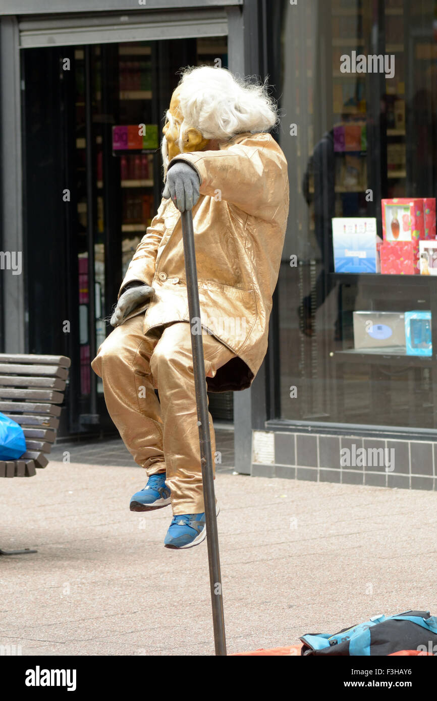 Street performer artist in painted gold suit with mask sat in mid-air ...