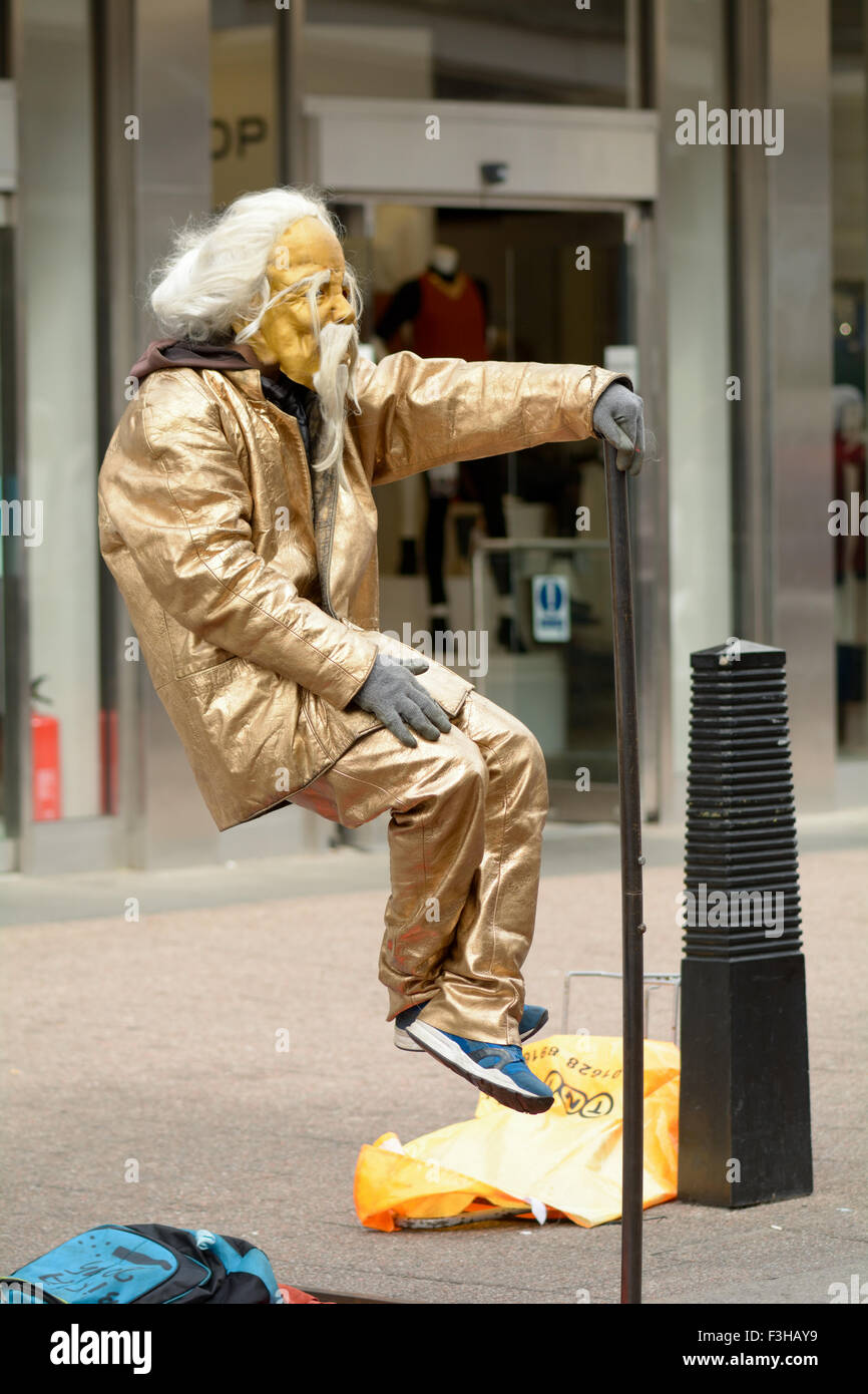 Street performer artist in painted gold suit with mask sat in mid-air ...