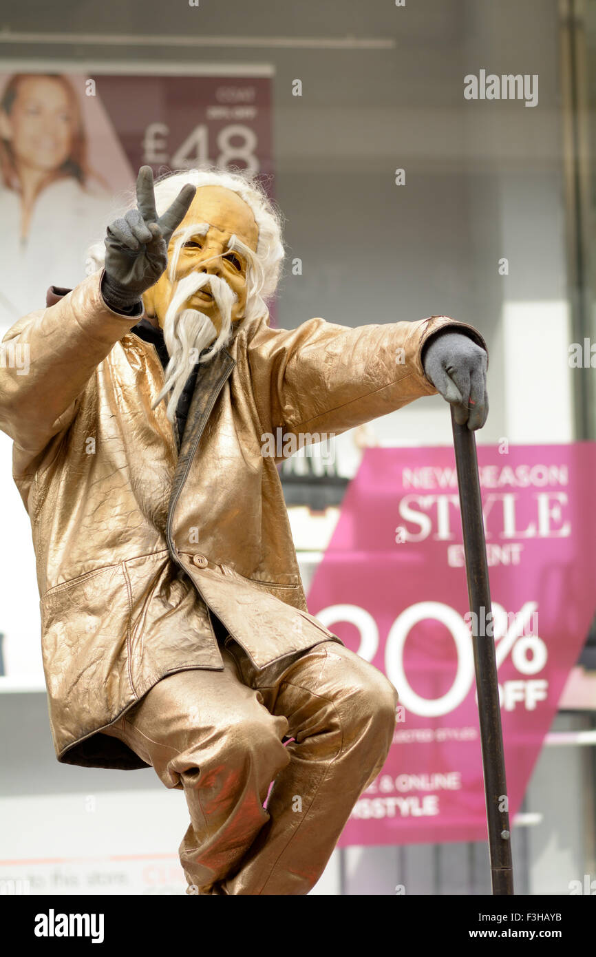 Street performer artist in painted gold suit with mask sat in mid-air ...