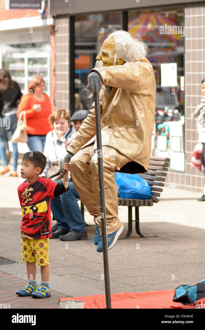 Street performer artist sat in mid-air on invisible perch holding boys ...