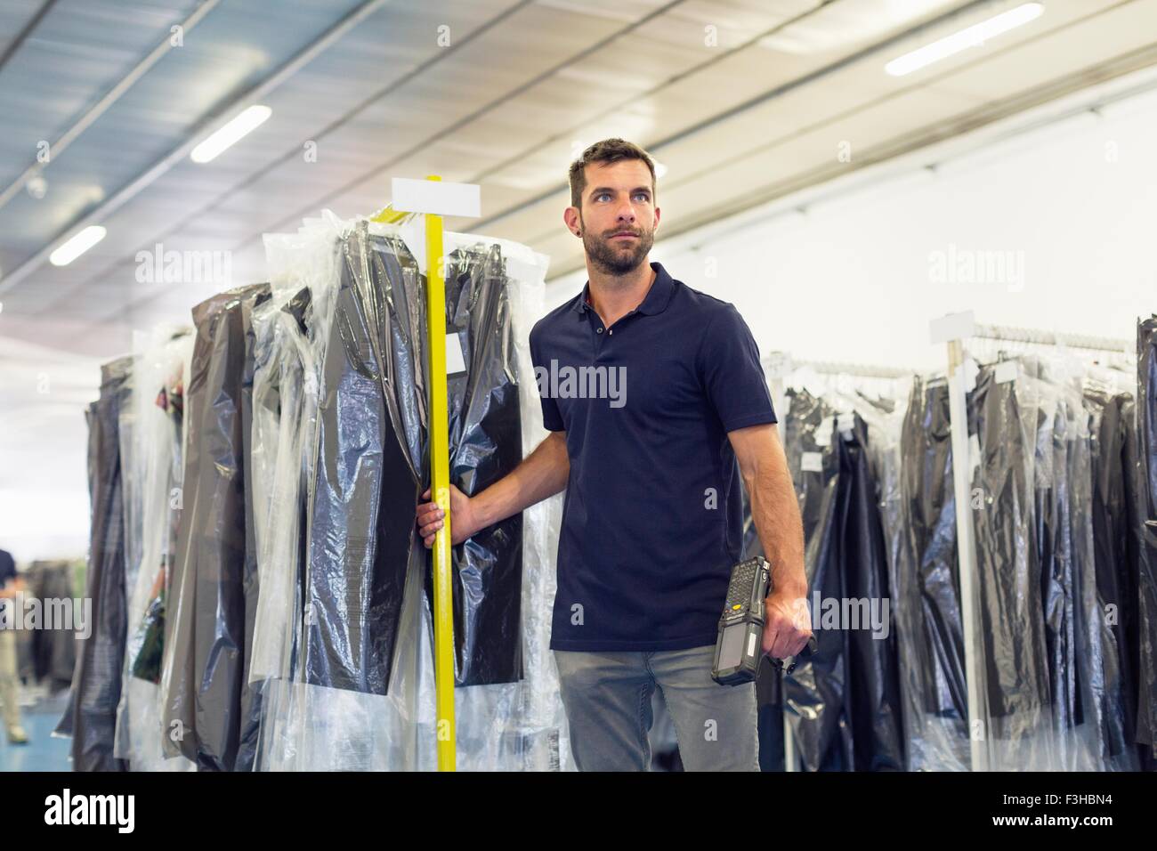 Warehouse worker pulling garment clothes rail in distribution warehouse ...