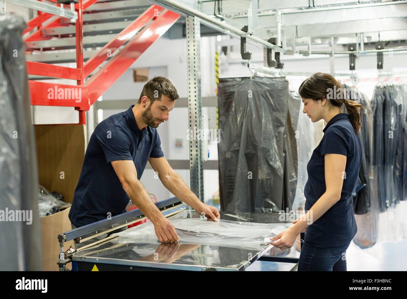 Warehouse workers wrapping garment stock in plastic in distribution ...
