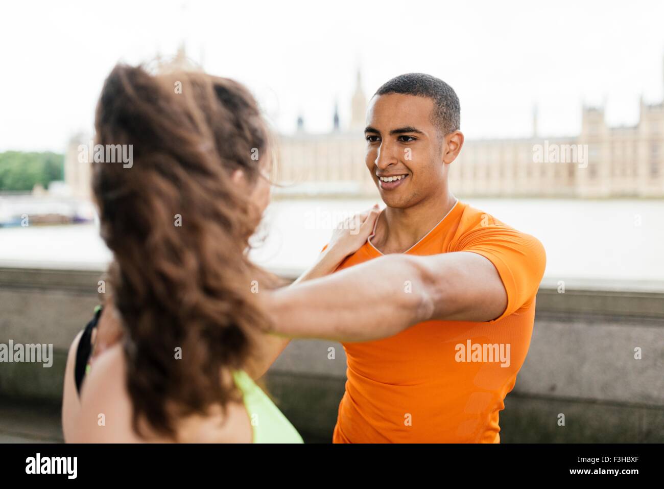 Over shoulder view of male and female runners warming up on riverside ...
