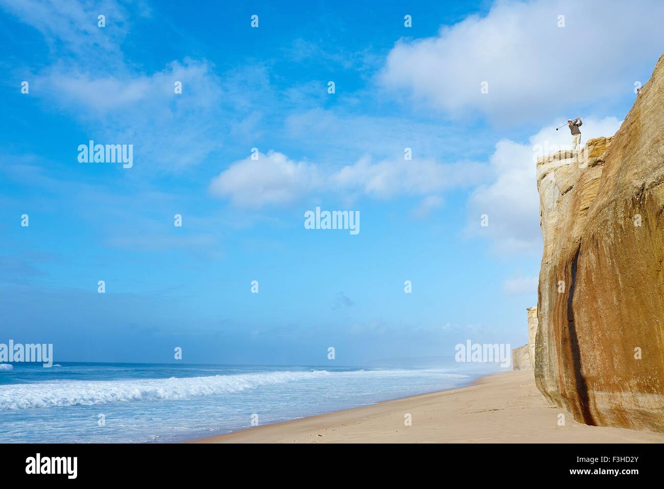 Low angle view of golder on cliff top overlooking beach taking golf ...