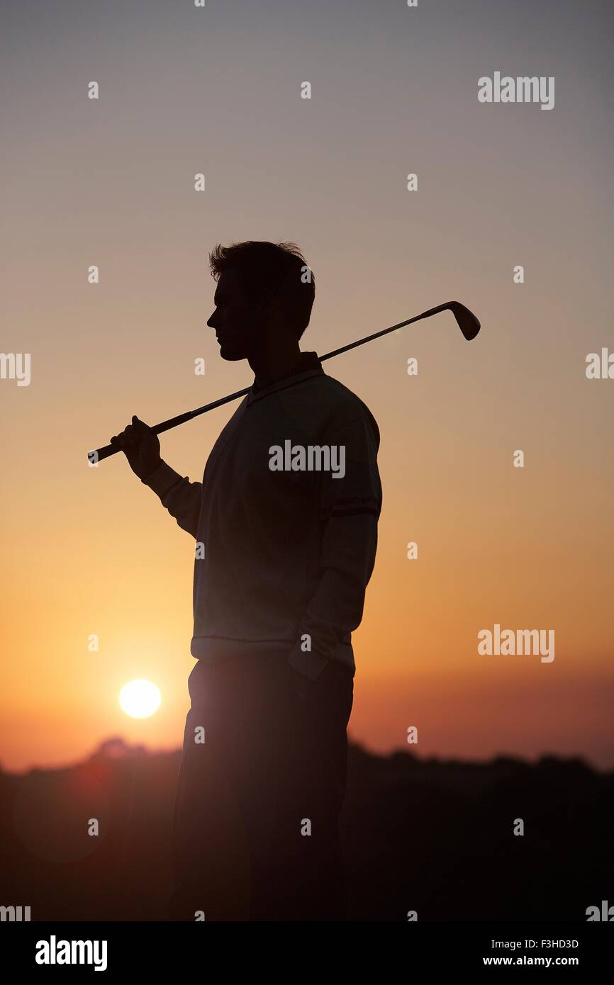 Golfer carrying golf club over shoulder in front of sunset, looking ...
