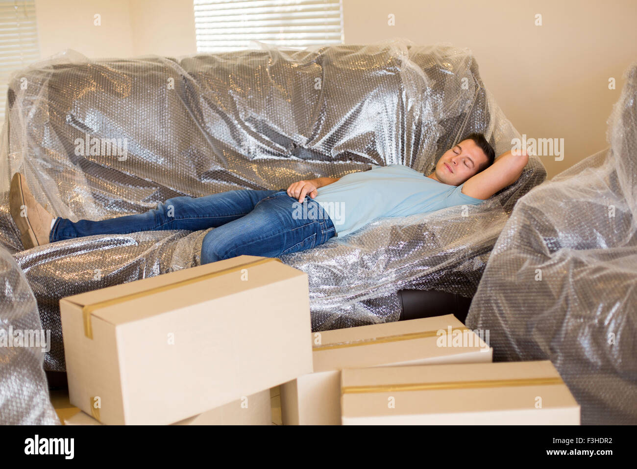 tired man sleeping on couch in new home with cardboard boxes around ...